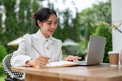 Premium Photo A Woman Using Her Laptop And Taking Notes On Her Notebook While Sitting At A