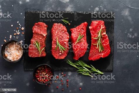 쇠고기 고기 어두운 슬레이트 또는 콘크리트 배경에 향신료 양파 로즈마리를 곁들인 신선한 소고기 스테이크 4개 맨 위 보기입니다 가루로 빻은에 대한 스톡 사진 및 기타 이미지