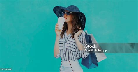 파란색 배경에 검은 둥근 여름 모자를 쓰고 쇼핑 백과 커피 컵을 가진 아름다운 젊은 여성의 초상화 여자에 대한 스톡 사진 및 기타 이미지 Istock