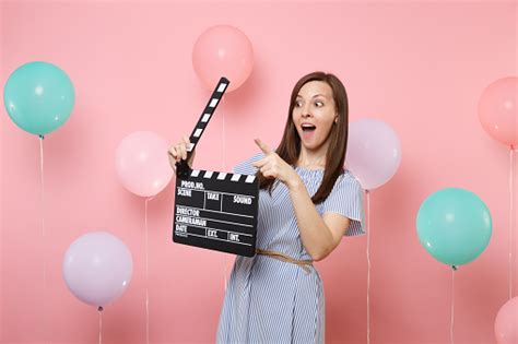 검지 손가락 옆으로 들고 클래식 블랙 필름 만들기 Clapperboard 화려한 공기 Baloons와 분홍색 배경에 가리키는 놀된 여자의 초상화 생일 휴가 파티 사람들이