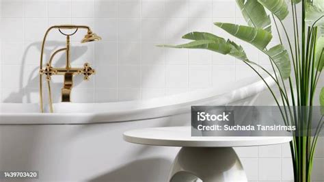 고급 디자인 욕실의 욕조 옆에 있는 흰색 원형 세라믹 사이드 테이블과 창문에서 얼룩덜룩한 햇빛이 비치는 열대 바나나 나무와 흰색 타일 벽에 나뭇잎 그림자가 있습니다 욕조에
