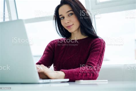 휴대용 장치에 앉아서 미소와 함께 카메라를 보고 매력적인 갈색 머리 Hipster 여자의 반 길이 초상화 세련 된 사무실 인테리어와 사용 하 여 컴퓨터에서 매력적인 학생