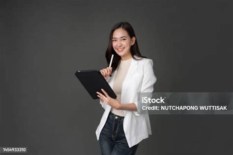 긴 소매에 흰색 코트를 입은 여성 임원 스튜디오에서 회색 배경을 배경으로 사진을 찍고 있다 그녀는 노트북 태블릿과 펜을 들고 있습니다 일어 서서 눈을 마주 치고 아름답게