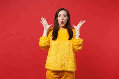 노란 털 스웨터 입 열어에 놀된 충격된 젊은 여자 스튜디오에서 밝은 빨간 벽 배경에 고립 손을 확산 사람들이 진심으 감정 라이프