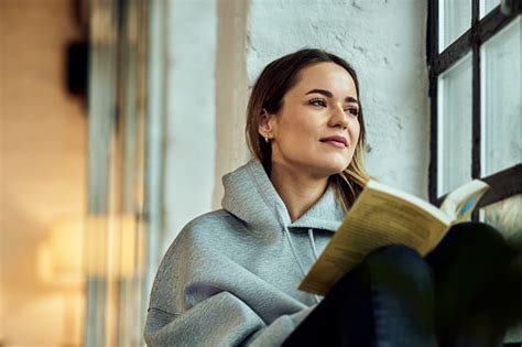 여자 창가에서 휴식을 취하고 책을 읽고 차분하게 미소 짓고 있습니다 30 34세에 대한 스톡 사진 및 기타 이미지 30 34세 Mental Wellbeing 고독