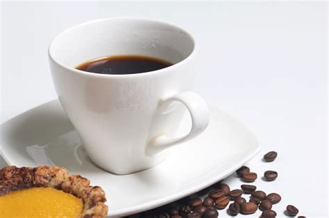 테이블의 흰색 표면에는 접시에 향기로운 커피 한 잔이입니다 근처 케이크가입니다 다음 흩어져있는 커피 콩 0명에 대한 스톡 사진