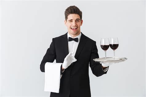 Premium Photo Handsome Young Waiter Wearing Tuxedo Holding Glass Of Red Wine Isolated Over