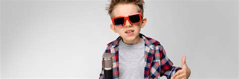 잘생긴 소년 격자 무늬 셔츠 회색 셔츠와 청바지에 회색 배경에 서 있다 선글라스를 착용 한 소년입니다 소년은 그의 손에서 마이크를 보유 하고있다 아이 랩 읽으십시오 개념에