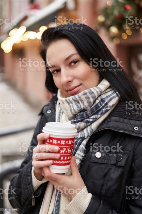 어깨 길이의 어두운 머리를 가진 아름다운 미소 소녀는 흐릿한 빛의 배경에 대해 거리에서 그녀의 손에 빨간 골판지 컵을 들고 30 34세에 대한 스톡 사진 및 기타 이미지