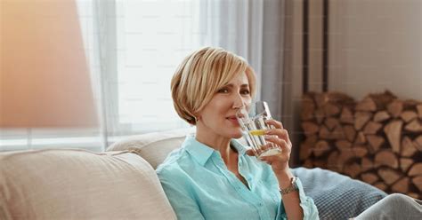 숙녀 음료 캐주얼 옷을 입은 중년 여성은 집에서 소파에 레몬 주스와 함께 신선한 물을 가지고 있습니다 건강한 식단의 개념 사진 Unsplash의 옛 이미지