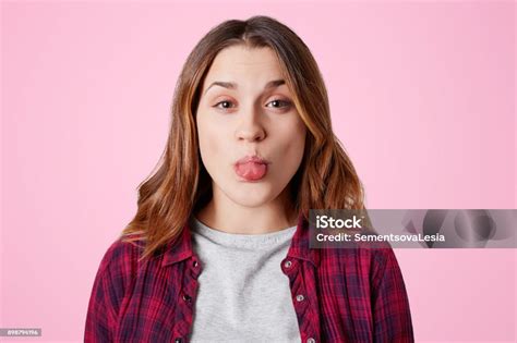재미 있은 예쁜 여 자가 Foolishes 실내 혀 얼굴을 찡 그리기 게 핑크 스튜디오 배경 위에 절연 체크 무늬 옷을 착용 귀여운 젊은 여성 재미 실내 카메라에 혀를 보여