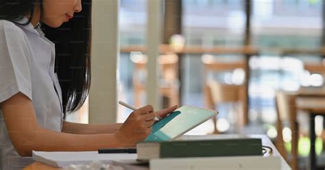 실험실 코트를 입은 여성 의사가 스타일러스 펜과 컴퓨터 태블릿을 손에 들고 나무 작업 책상에 앉아 있는 동안 자른 이미지 사진 Unsplash의 책 더미 이미지