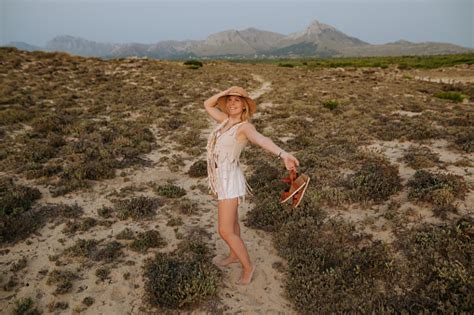 여름 모자를 쓰고 마요르카의 녹색 모래 언덕 과 배경의 아름다운 산악 풍경 사이에 서있는 보헤미안 옷을 입은 행복한 금발 젊은 여성 Mental Wellbeing에 대한