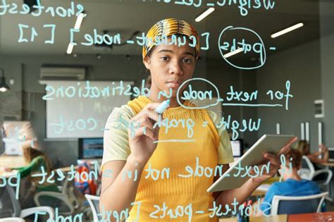 black woman writing computer code on glass wall in classroom stock