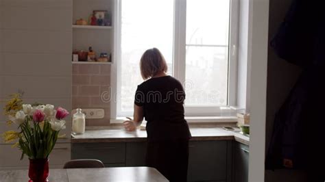Woman Tidying Up The Kitchen Table And Organizing Spaces Back View