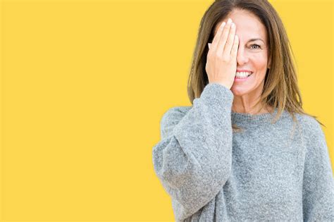 아름 다운 중 년 여자 얼굴과 놀라운 감정에 확신 미소와 함께 손으로 한쪽 눈을 덮고 격리 된 배경 위에 겨울 스웨터를 입고 가리기에 대한 스톡 사진 및 기타 이미지