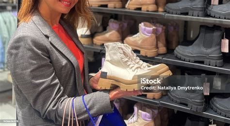 웃고 있는 성인 여성이 손을 잡고 가을 신발을 카메라에 보여주는 클로즈업 매장에서 베이지색 부츠를 선택하는 긍정적인 여성 구매자 옷을 사십시오 패션 개념입니다 가방에 대한