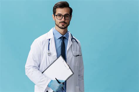 흰 코트와 안경을 쓴 남자 의사 의료 기록과 청진기가 있는 파란색 고립된 배경 복사 공간 텍스트 공간에 미소를 짓고 있습니다 25 29세에 대한 스톡 사진 및 기타 이미지