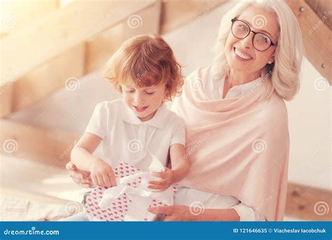 Joyful Granny Smiling Into Camera While Her Grandson Opening T Stock