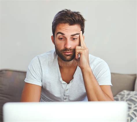 This Is So Boringa Handsome Young Man Looking Bored While Working On His Laptop At Home