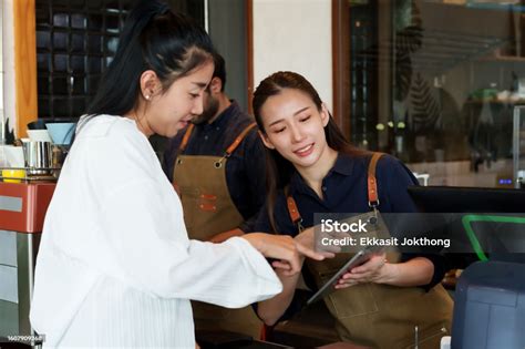 아시아 여성 바리스타 가게에서 정기적으로 커피를 주문하는 아름다운 고객의 주문을 받습니다 그리고 그의 남편은 작은 커피숍 가족 사업에서 바 카운터 뒤에서 바리스타로 일하고