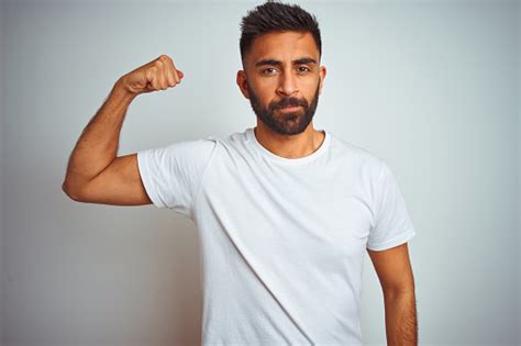 고립된 흰색 배경 위에 서있는 티셔츠를 입은 젊은 인도 남자 팔 근육 자신감과 자랑스러운 힘을 보여주는 강한 사람 T 셔츠에 대한 스톡 사진 및 기타 이미지 Istock