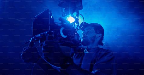 캐주얼웨어를 입은 젊은 남자가 비디오 카메라를 들고 푸른 빛으로 불을 밝히고 연기로 가득 찬 스튜디오에서 광고를 촬영하고 있다 사진 Unsplash의 어둠 이미지