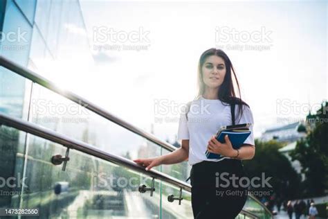 휴식 시간에 도시 환경에서 포즈를 취하는 교육 장비를 손에 든 매력적인 여학생의 절반 길이 초상화 지식 교과서를 들고 있는 20세의 아름다운 백인 학생 학생에 대한 스톡