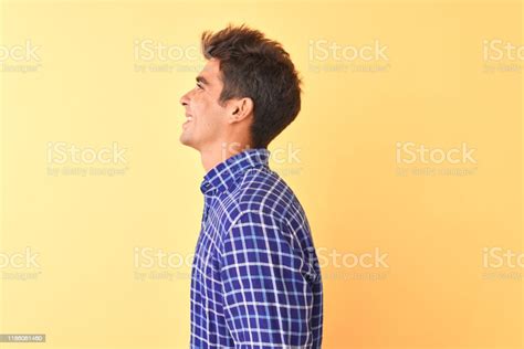 옆으로 찾고 고립 된 노란색 배경 위에 서있는 캐주얼 셔츠를 입은 젊은 잘생긴 남자는 자신감있는 미소로 자연스러운 얼굴로 프로필 포즈를 취합니다 남자에 대한 스톡 사진 및