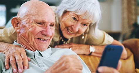 시니어 커플 전화 및 포옹과 함께 소파에서 읽기 비디오로 선택 및 클릭 다운로드 또는 집에서 검색 나이 든 여성 남자 스마트폰이 라운지 소파에 앉아 소셜 미디어에 게시하기