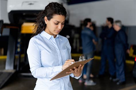 역학의 팀이 배경에 서있는 동안 목록에 서비스를 확인하는 아름다운 여성 조수 자동차 수리 공장에 대한 스톡 사진 및 기타 이미지 자동차 수리 공장 접수원 경영자
