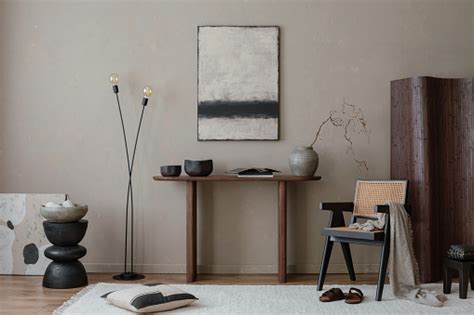 모형 포스터 프레임 나무 콘솔라 세련된 램프 등나무 안락 의자 베이지 색 깔개 가지가 달린 꽃병 및 개인 액세서리가있는 따뜻한 거실 인테리어의 창의적인 구성 가정 장식 템