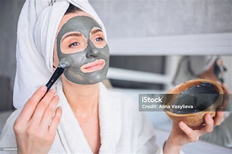 아름다운 미소 여자 에 집에서 목욕 가운 에 수건 적용 얼굴 점토 마스크를 적용 여드름에 대 한 문제 피부를 젊어지게 가정 생활에 대한 스톡 사진 및 기타 이미지 Istock