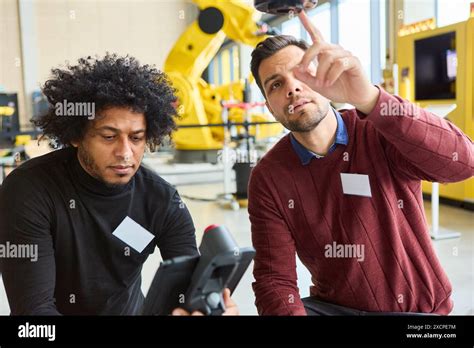 Two Engineers Collaborate On Programming A Robotic Arm In An Industrial