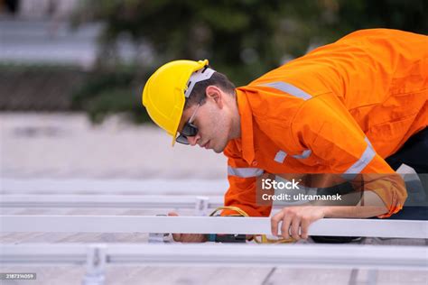 주황색 안전복과 헬멧을 착용한 옥상에서 도구를 사용하여 금속 프레임을 설치하는 기술자 옥상 건설 및 재생 에너지 프로젝트에 대한 정밀도 안전 및 전문 지식을 묘사합니다 건설