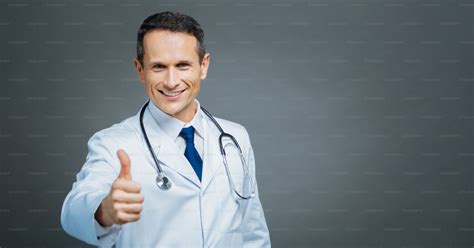 모든 것이 멋지다 똑바로 서서 엄지 손가락 한숨을 쉬면서 얼굴에 밝은 미소를 지으며 카메라를 바라 보는 쾌활한 남자 의사의 허리 업 샷 사진 Unsplash의 인체