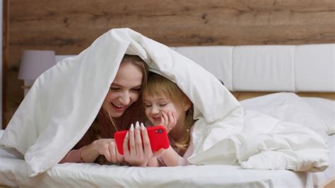 어머니는 만화를보고 휴대 전화를 들고 딸 아이 소녀와 이불 담요 아래 침대에 누워 2명에 대한 스톡 사진 및 기타 이미지 2명 가리기 가정 생활 Istock