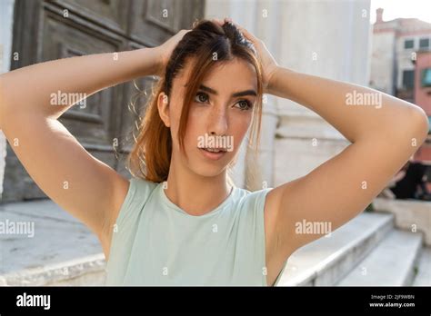 Portrait Of Redhead Woman Posing With Hands Behind Head On Blurred