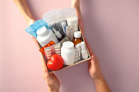 분홍색 배경에 알약 병 마스크 하트 모양의 물체 등 다양한 의료용품이 담긴 상자를 들고 있는 손 응급 처치 의료 기부 상자 개념 2명에 대한 스톡 사진 및 기타 이미지