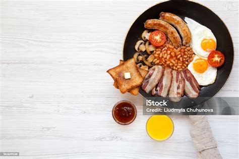 전통적인 전체 영어 아침 식사 달걀 프라이 베이컨 소시지 콩 토스트와 복사 공간 평면도와 흰색 나무 바탕에 오렌지 주스와 함께 냄비 플랫이 하다 위에서 0명에 대한 스톡