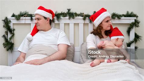 크리스마스와 새해를 위해 장식 된 침대에서 아기와 남편과 아내의 싸움 가정 침실에있는 가족 커플 3 명에 대한 스톡 사진 및