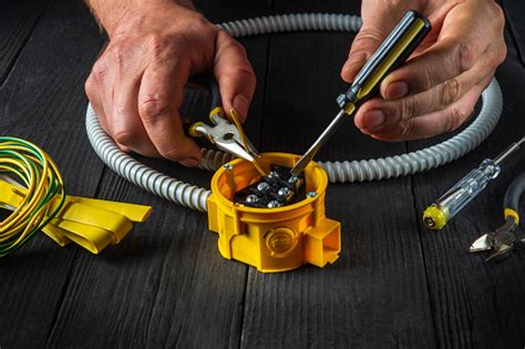 마스터 전기 기술자의 작업장에서 전기 연결 작업 중 마스터 전기 기술자의 손 클로즈업 노란색 정션 박스에 케이블 또는 와이어 설치 개체 그룹에 대한 스톡 사진 및 기타