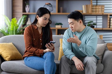 스마트폰으로 소파에서 진지한 대화를 나누는 아시아 커플 전화기를 들고 있는 여자에게 무언가를 설명하는 남자 거실 환경에서 활발한 커뮤니케이션과 현대 기술을 만나보세요 2명에