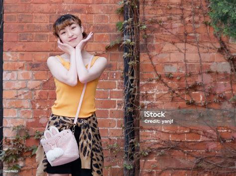 노란색 홀터 상단과 짧은 치마에 행복 한 중국 여자의 초상화 포즈와 붉은 벽돌 벽 배경으로 미소 매력적인 중국 세련된 여성의 패션 초상화입니다 아름다움과 라이프 스타일 개념