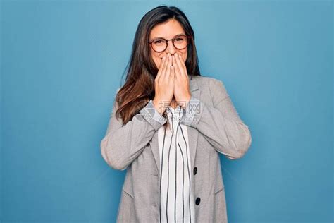 带着眼镜站在蓝色孤立背景面前的年轻西班牙女商人大笑和尴尬的笑脸高清图片下载 正版图片506579229 摄图网