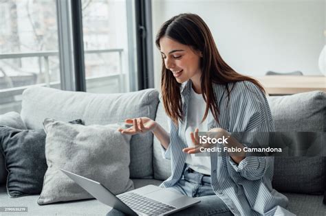 웃는 소녀는 집에서 소파에 앉아서 노트북에서 화상 통화를하는 친구나 가족과 손을 흔들며 이야기하고 행복한 젊은 여자는 인사하고 인사하고 말하고 컴퓨터에서 데이트 온라인 응용