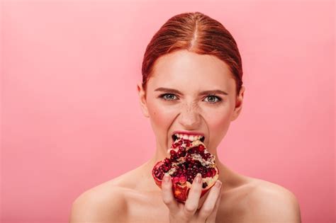 석류를 먹는 배고픈 여자의 전면 모습입니다 분홍색 배경에 고립 된 가닛과 벌 거 벗은 생강 소녀의 스튜디오 샷 무료 사진