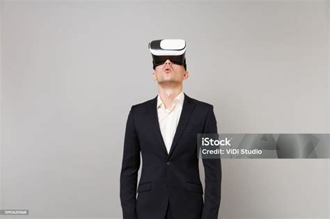 클래식 블랙 정장에 흰 셔츠 스튜디오에 회색 벽 배경에 고립 된 헤드셋에서 찾고 젊은 사업가의 초상화 성과 경력 부 비즈니스 개념입니다 복사 공간을 비웃는 다 검은색에 대한