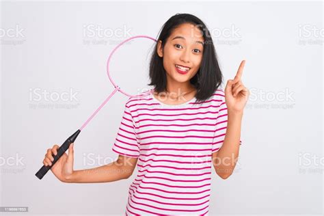 젊은 아름다운 중국 여자 들고 배드민턴 라켓 위에 고립 된 흰색 배경 에 놀란 아이디어 또는 질문 가리키는 손가락으로 행복한 얼굴 번호 하나 가리키기에 대한 스톡 사진 및
