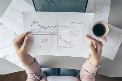 맨 위 보기 커피 한 잔을 들고 테이블에 앉아 종이에 인쇄 된 그래픽과 차트가있는 노트북에서 일하는 젊은 비즈니스 여성 거래자에 대한 스톡 사진 및 기타 이미지 Istock